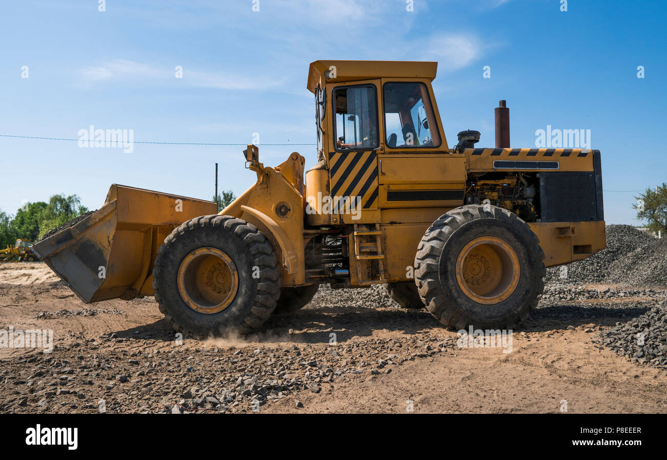 Yellow loader moving with uploaded bucket with stone gravel during road ...