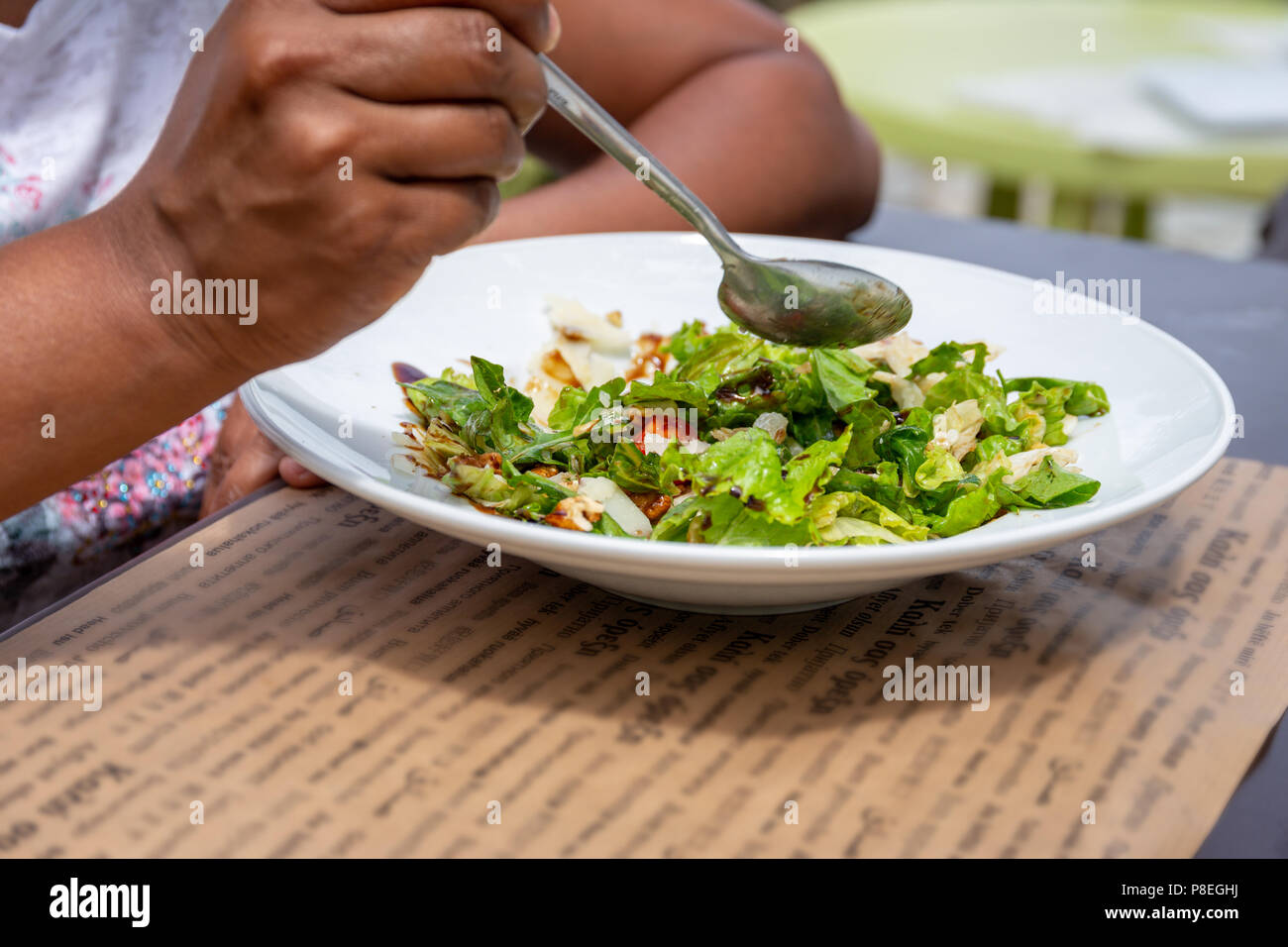 A young woman eating a bowl of fresh, healthy salad, dressed with ...