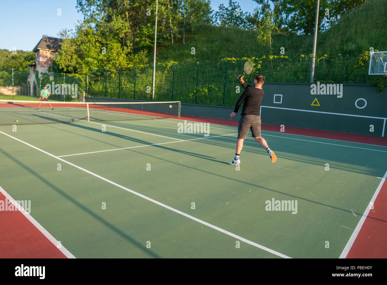 Man is playing tennis on tennis court outdoors in sunset Stock Photo ...