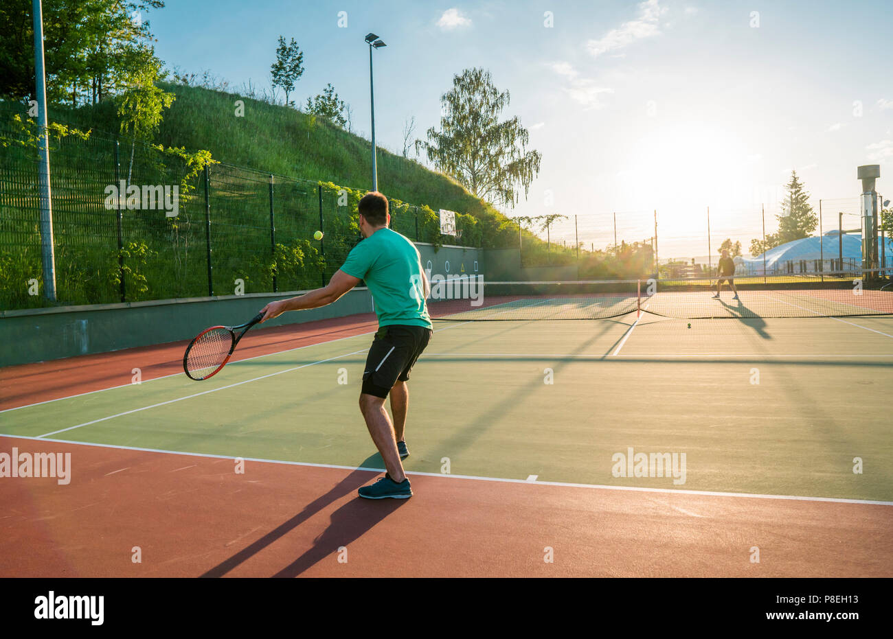 Man is playing tennis on tennis court outdoors in sunset Stock Photo ...