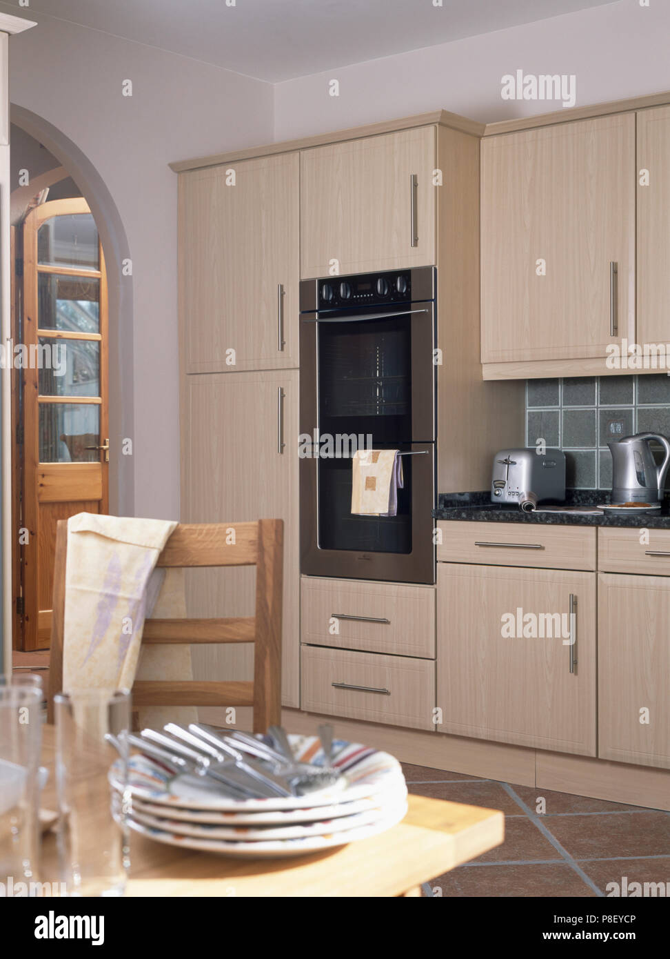 Cutlery and plates on table in modern kitchen with light wood units ...