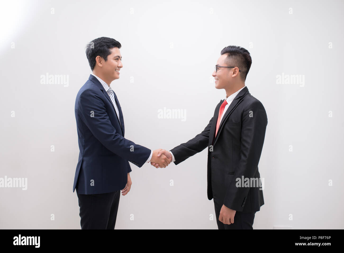 Side view of two smiling young businessmen shaking hands in white ...