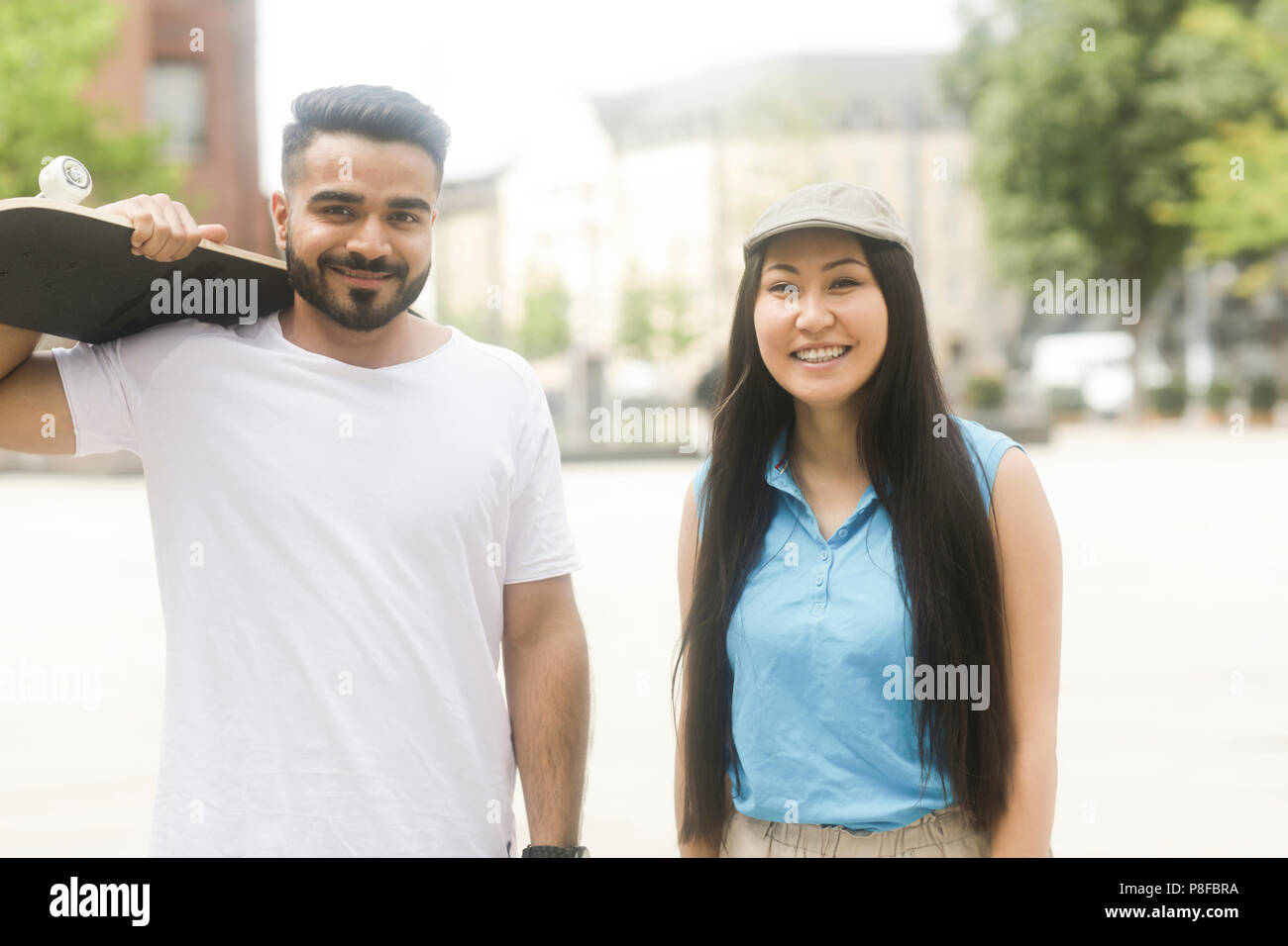 Couple standing in a city square with their skateboard Stock Photo - Alamy