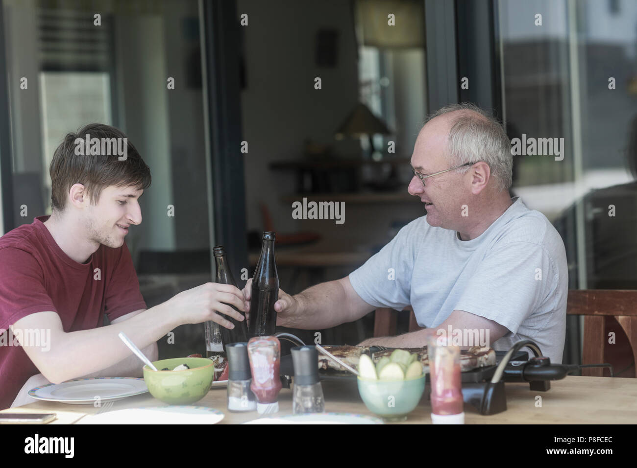 Adult father and son sitting on terrace making a celebratory toast ...