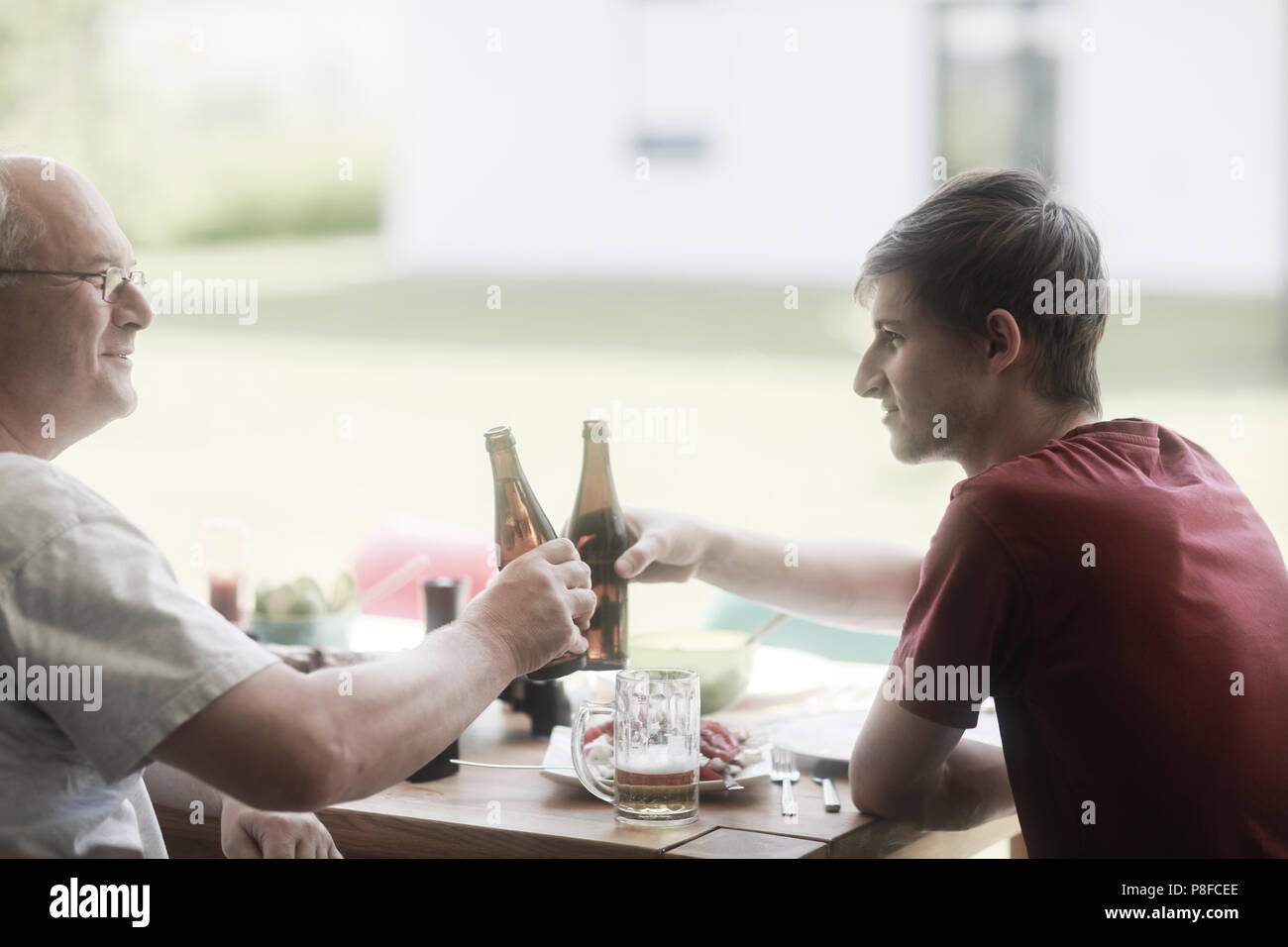 Adult father and son sitting on terrace making a celebratory toast ...