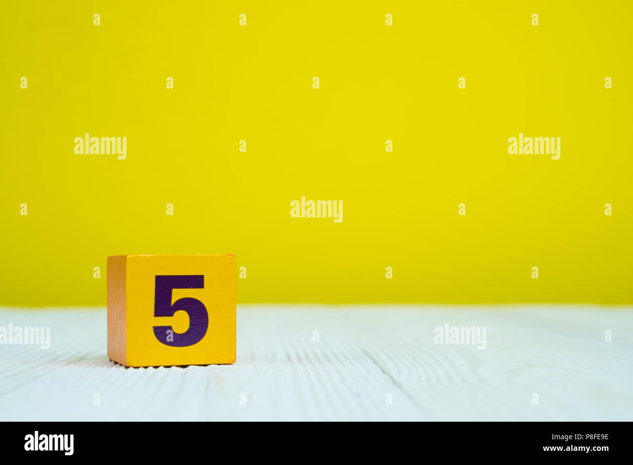 Square block puzzle number 5 on table with yellow wall background Stock ...