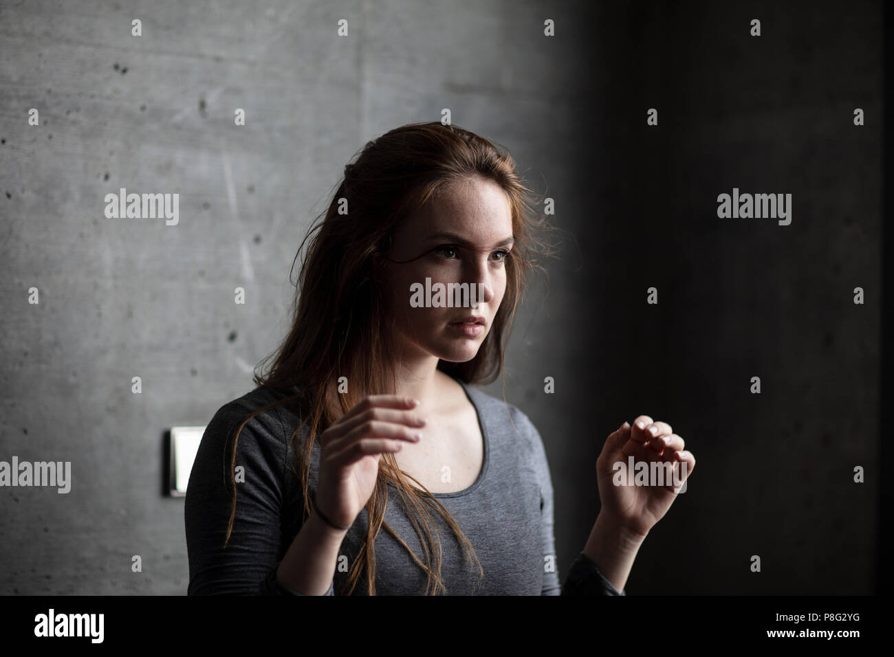 Young woman raising her arms standing behind a grey concrete wall ...