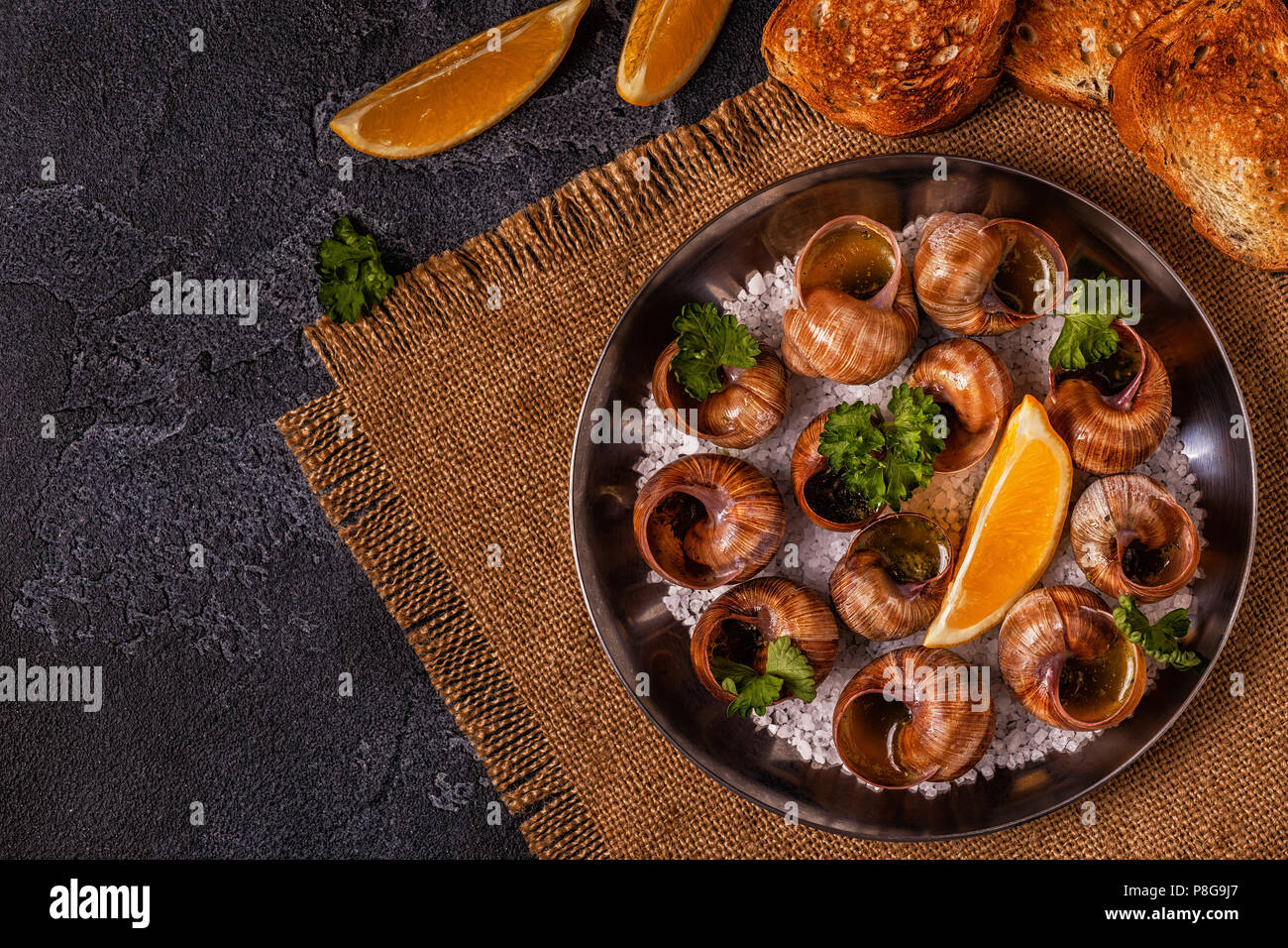 Fried snails with lemon, baguette and parsley, top view Stock Photo - Alamy