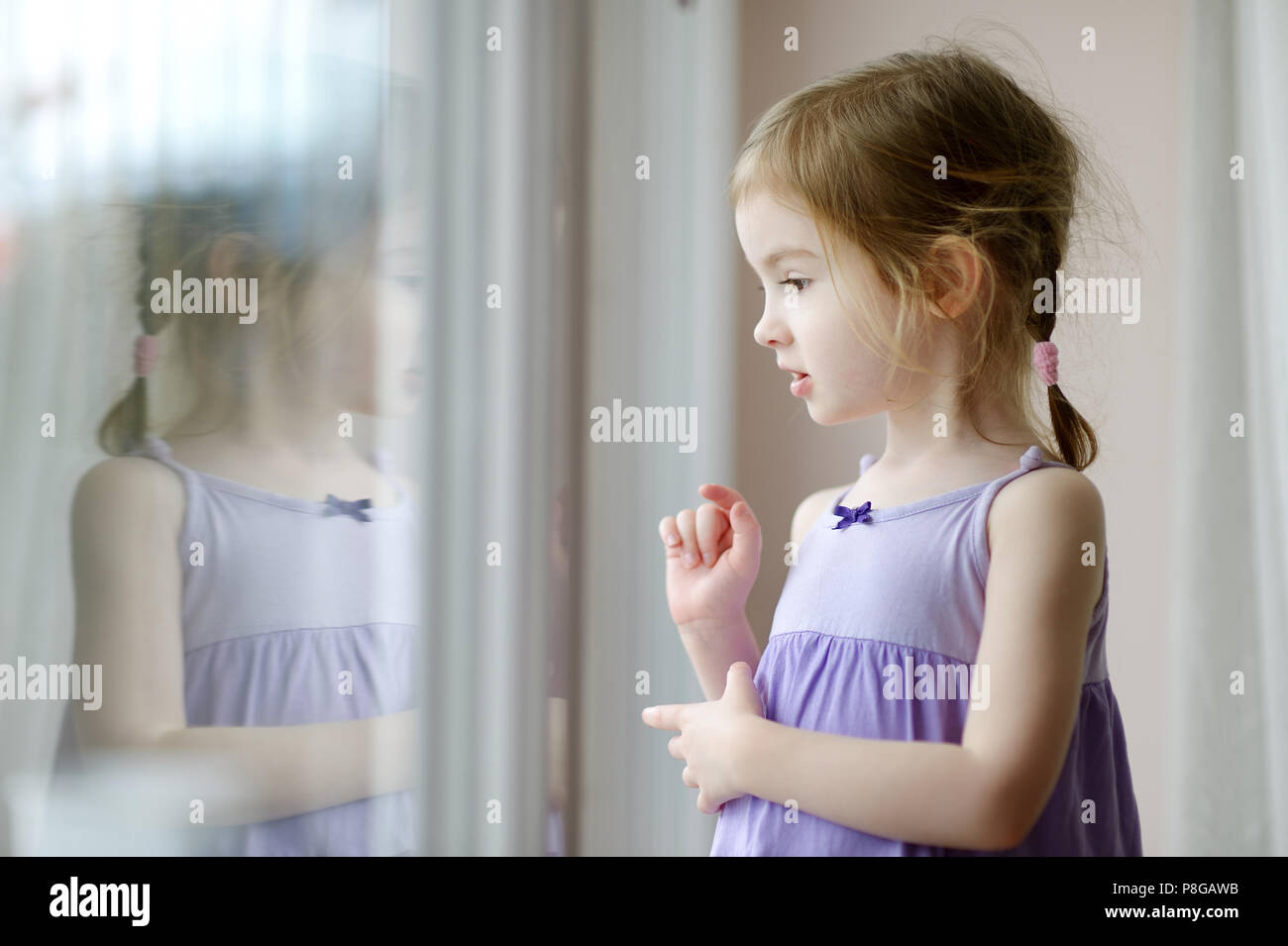 Adorable little girl looking through the window Stock Photo - Alamy