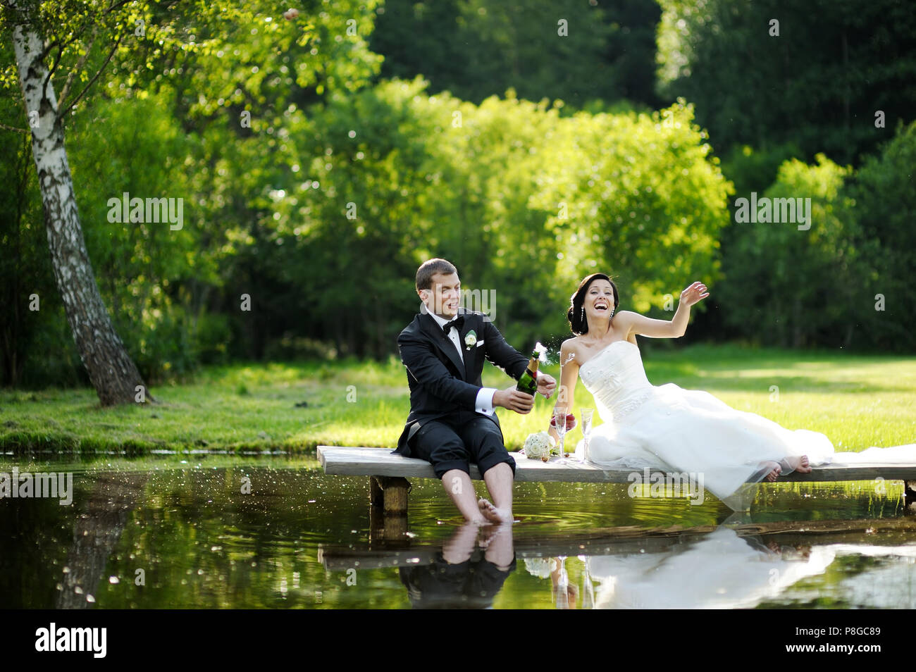 Bride and groom drinking champagne by the lake Stock Photo - Alamy