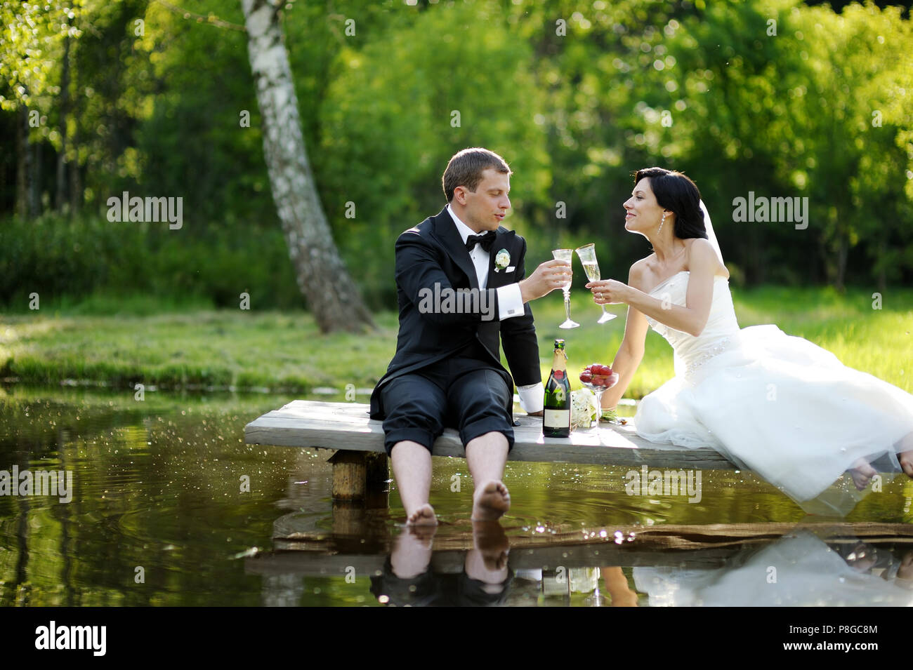 Bride and groom drinking champagne by the lake Stock Photo - Alamy