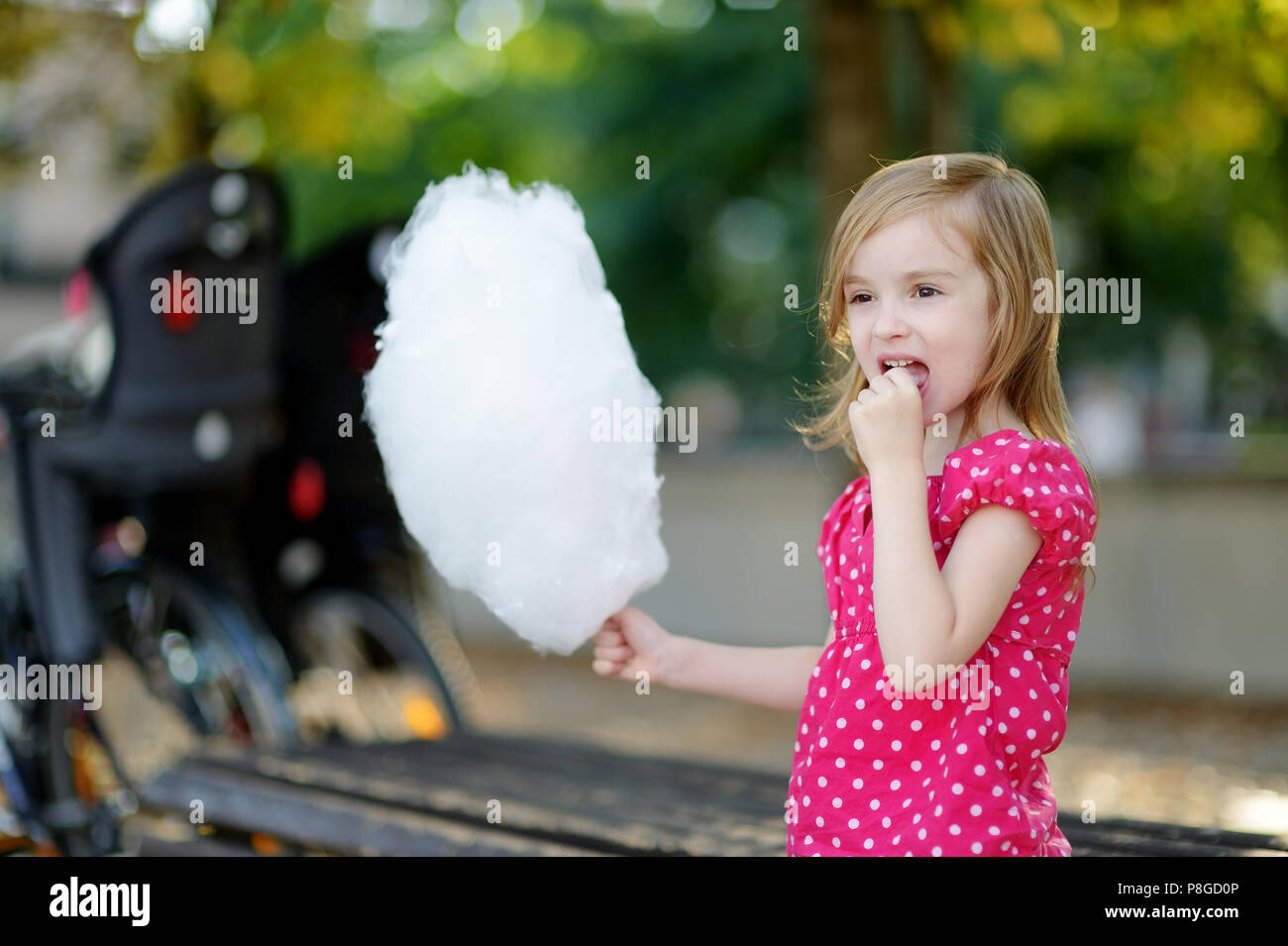 Adorable little girl eating candy-floss outdoors at summer Stock Photo ...