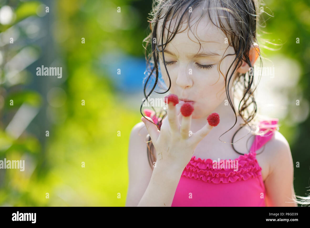 Adorable little girl eating raspberries off her fingers Stock Photo - Alamy