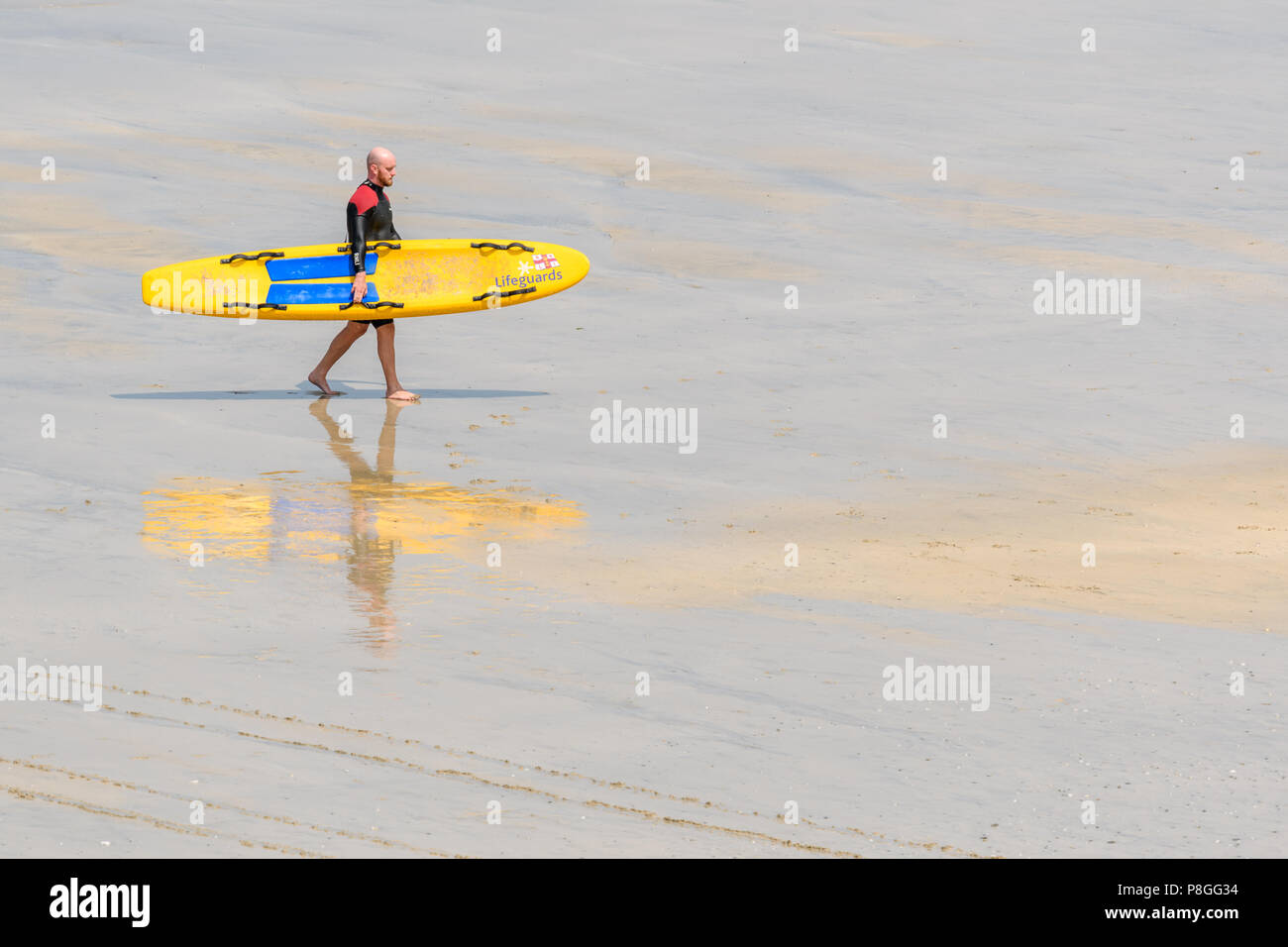 A male lifeguard with surfboard walks along the shore of the Atlantic ...