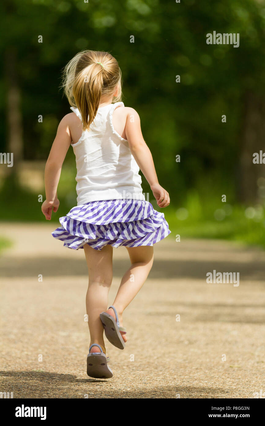 Young female child skipping on a rock path in the spring time. Back is ...