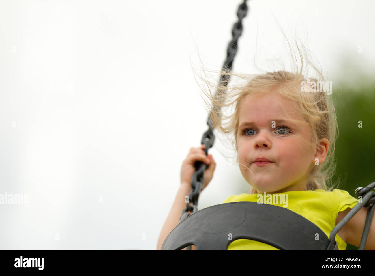 Young female child having fun at a playground on the swings. Copy space available on the left ...