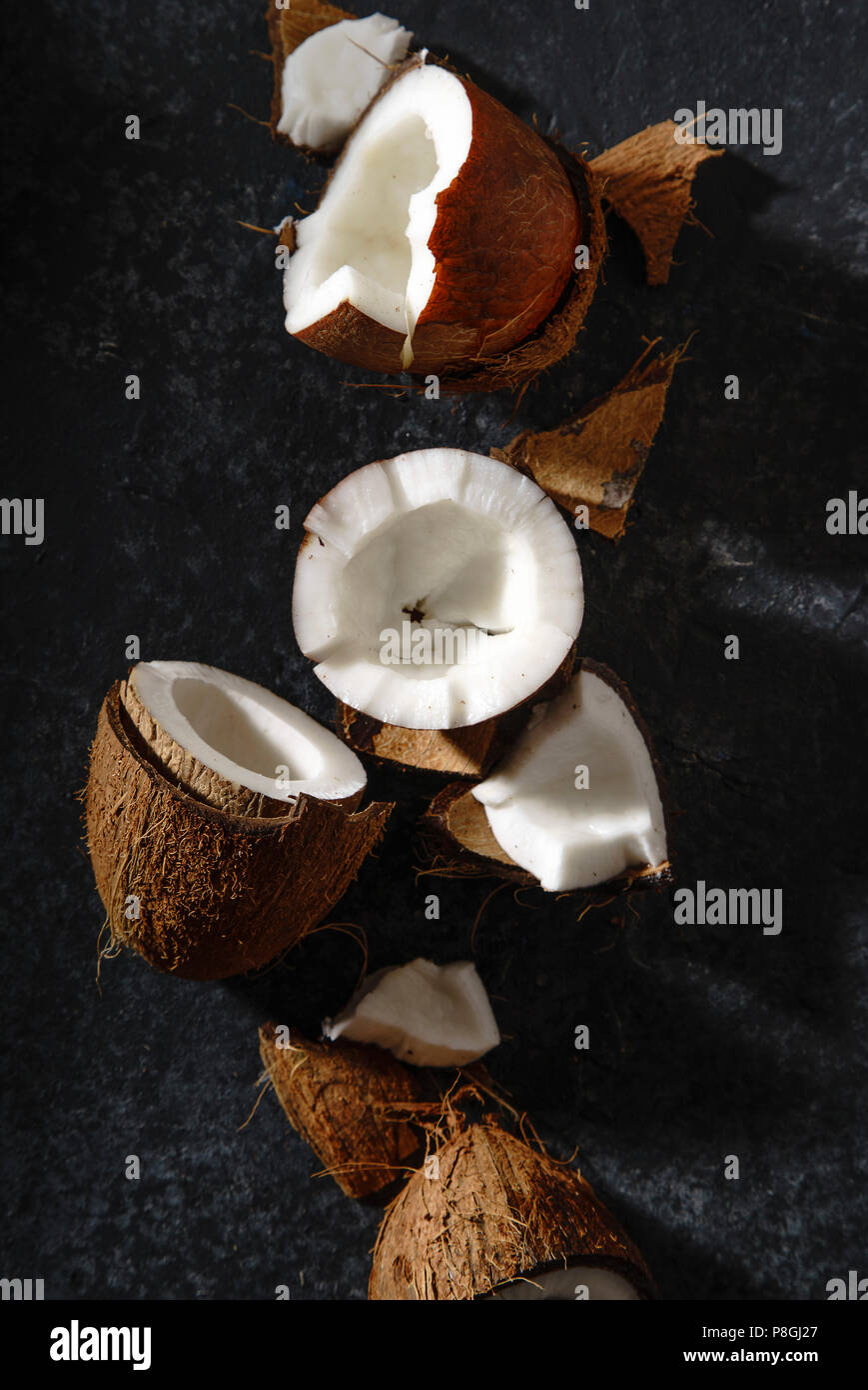 Close up image of cracked coconuts arranged on dark textured background ...