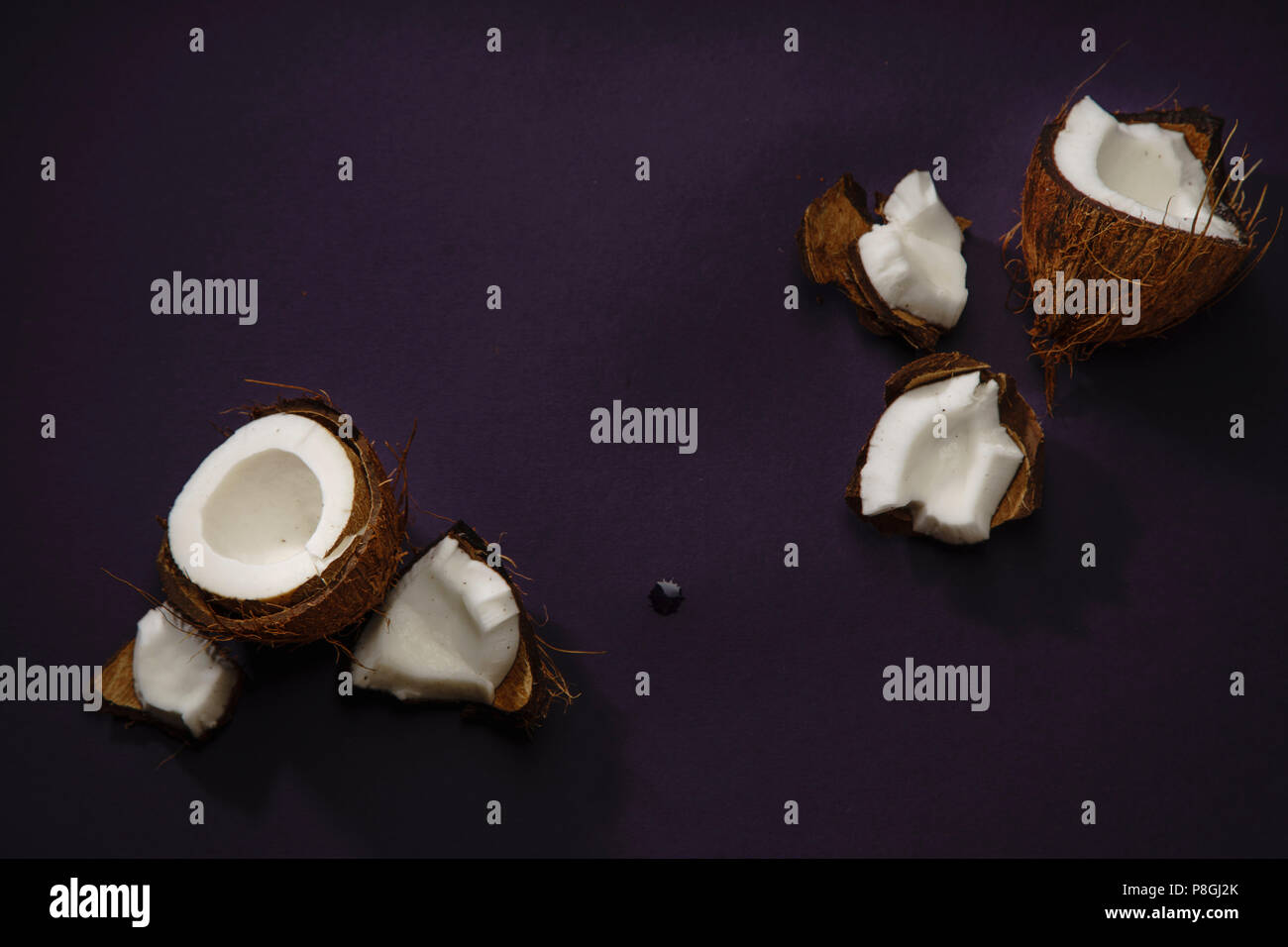 Cracked coconut arranged on dark purple background with copy space ...