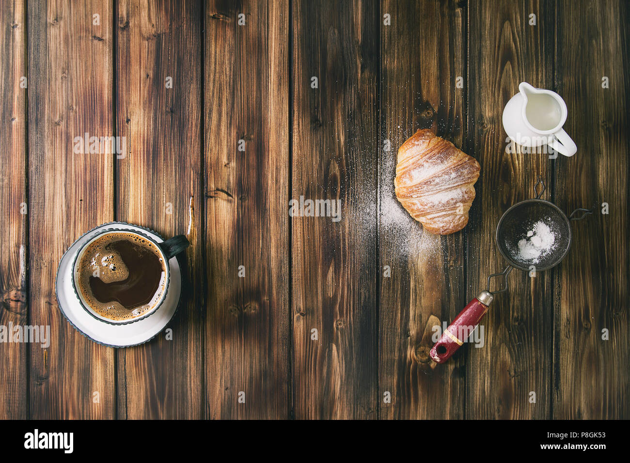 Homemade croissant with sugar powder, cup of coffee, jug of milk ...