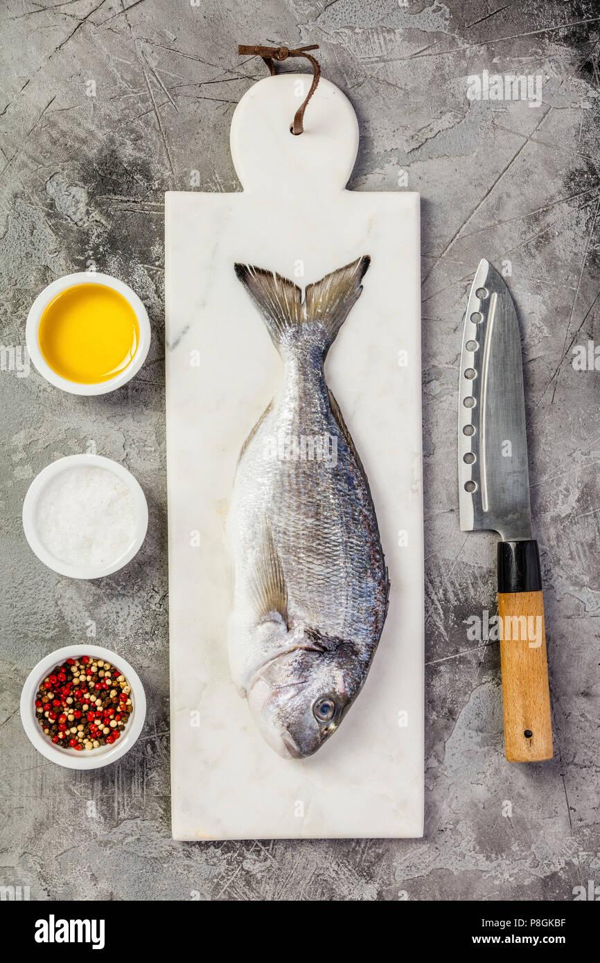 Delicious fresh sea bream fish on marble board, herbs and spices over ...
