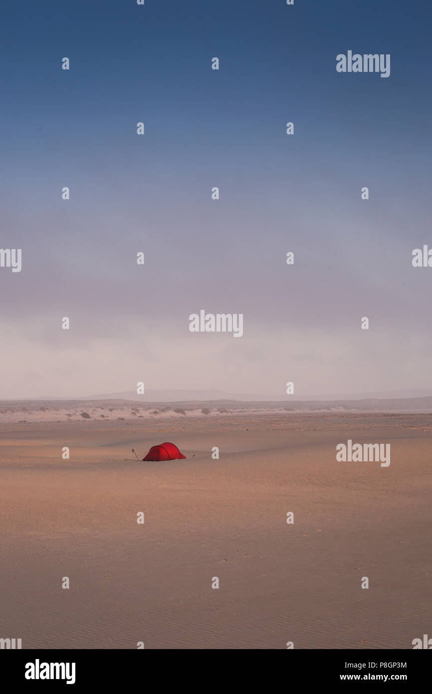 Red tent on a vast open sand field with dunes all around in a desert ...
