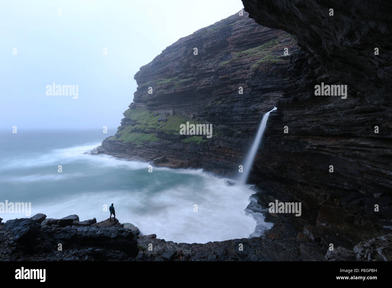 Man looking a a big waterfall falling straight into the ocean at ...
