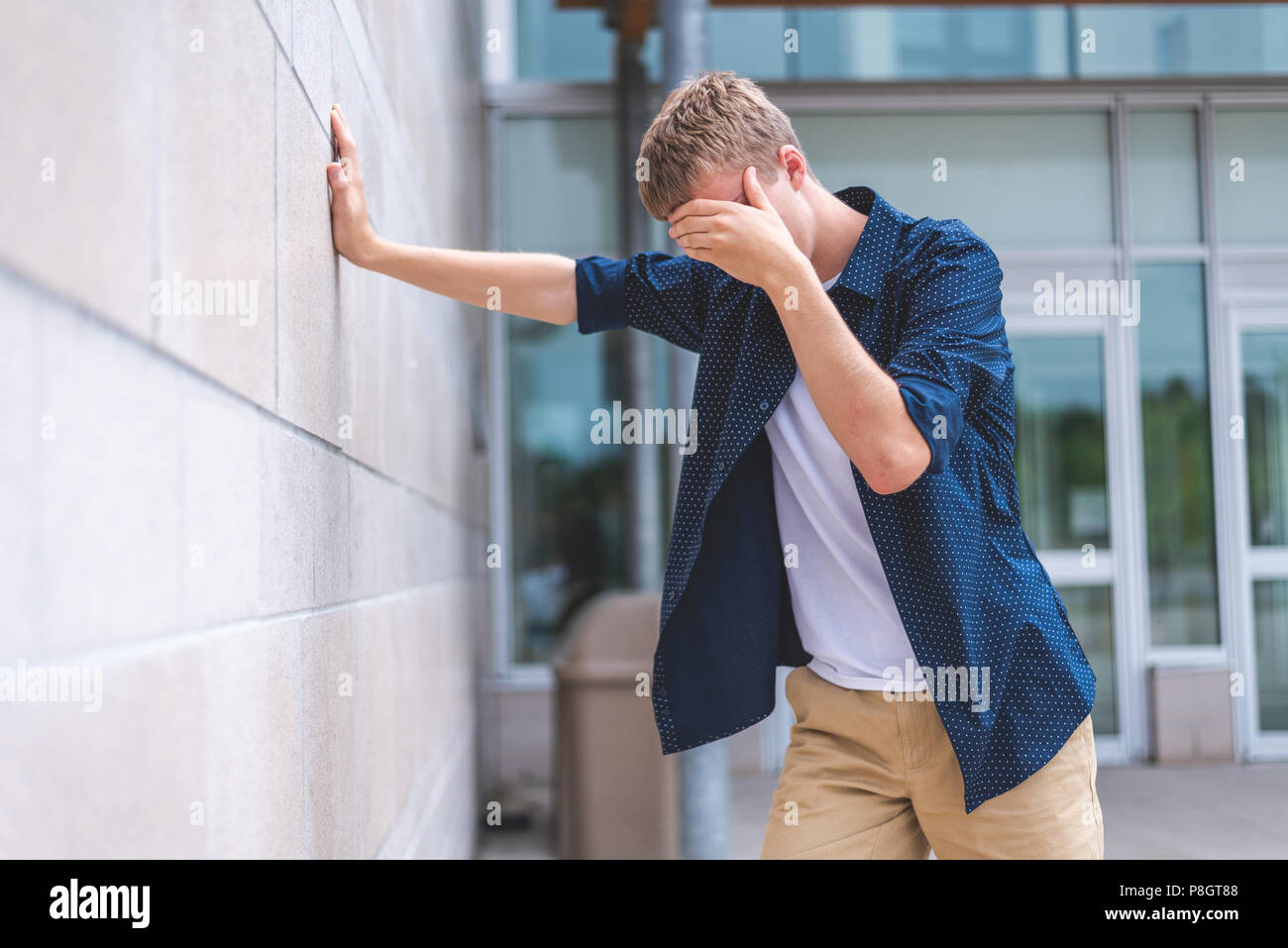 Upset teen leaning against a brick wall outside of a public building ...