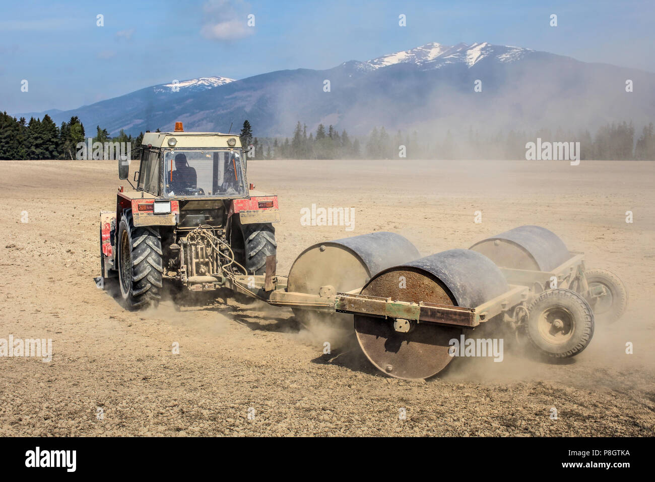 Tractor pulling heavy metal rollers on a dry field with mountains in ...