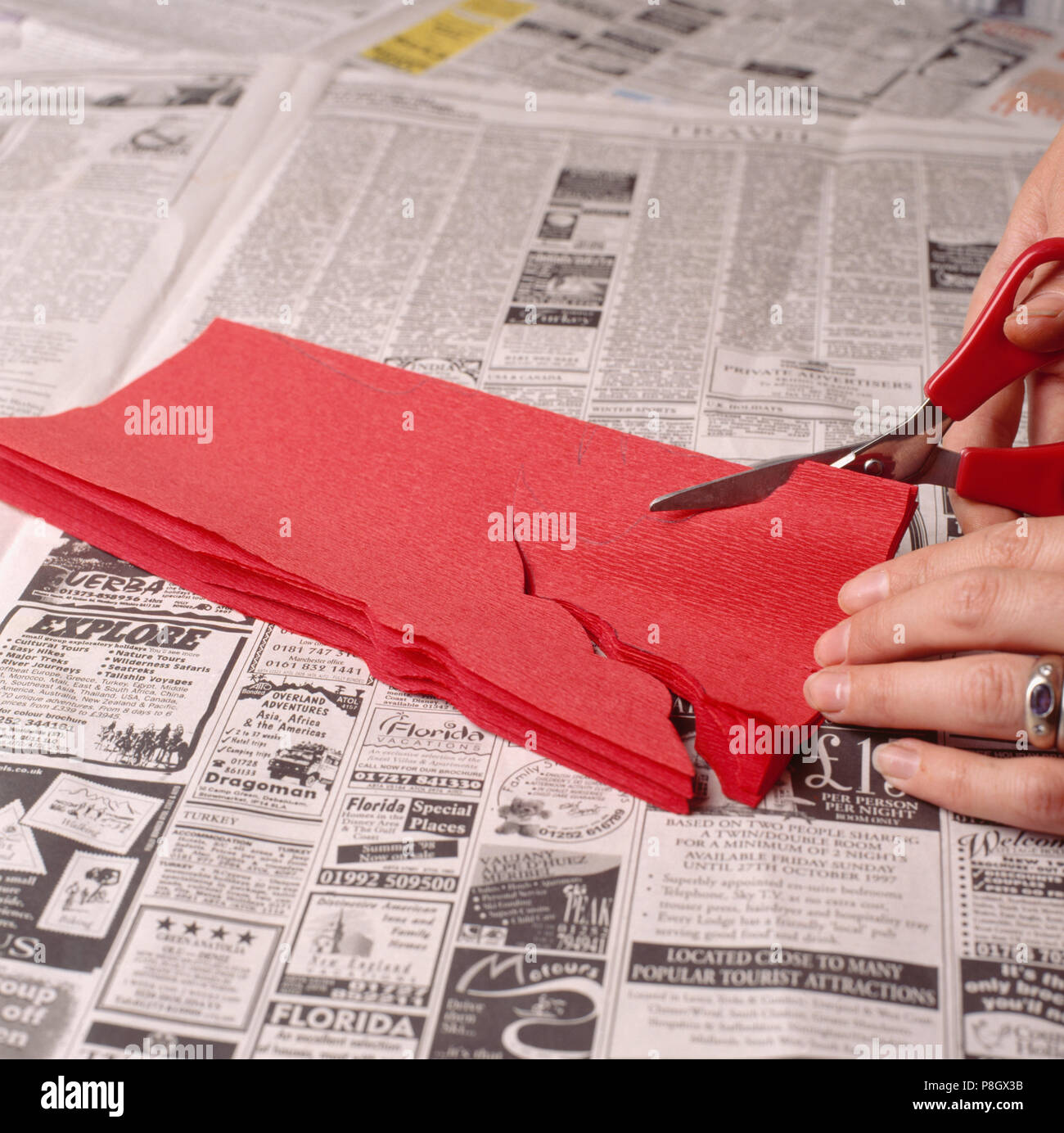 Close-up of hands using scissors to cut out pattern in folded red crepe ...