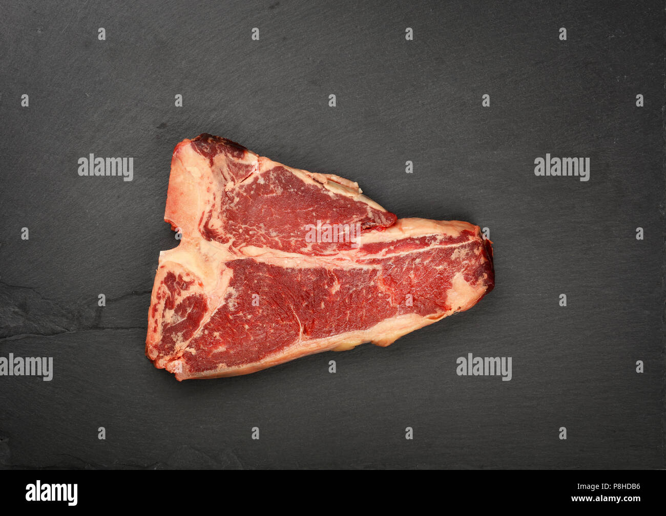 Close up one raw T-bone beef steak with rib bone on black slate board ...
