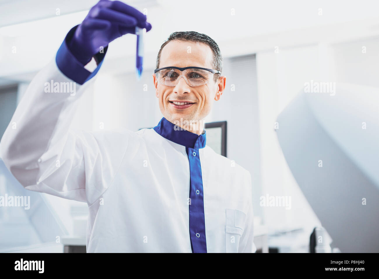 Positive delighted lab assistant checking blue liquid Stock Photo - Alamy
