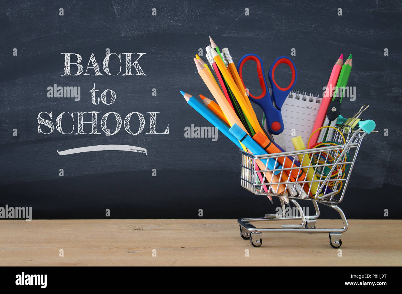 Shopping cart with school supply in front of blackboard. Back to school ...