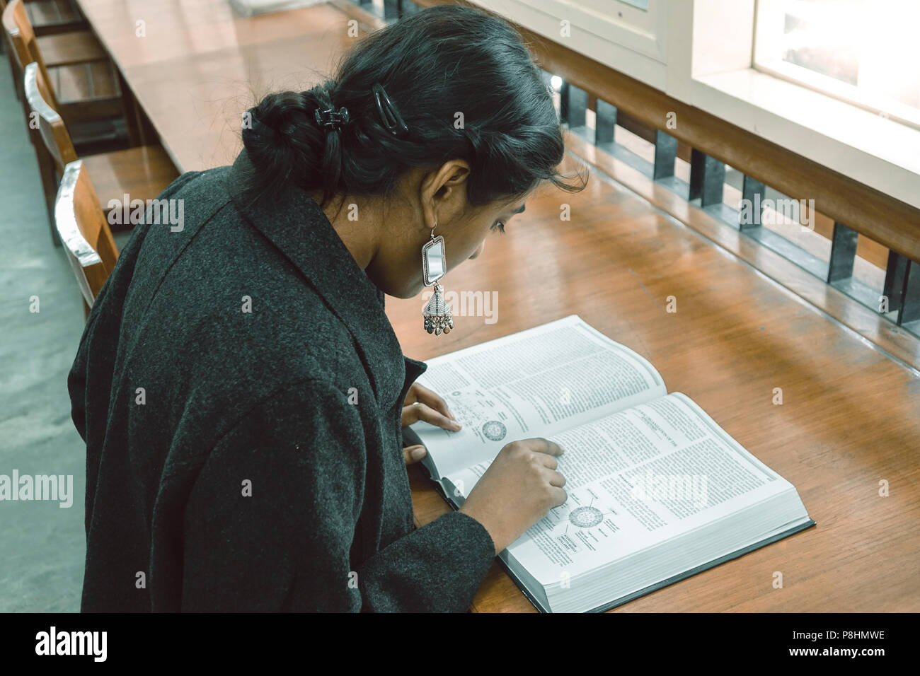A young Indian woman professor studying books on the table desk of the ...