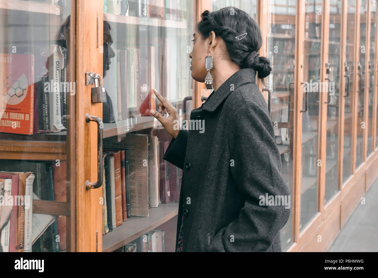 A young Indian woman professor looking for books in the shelf of ...