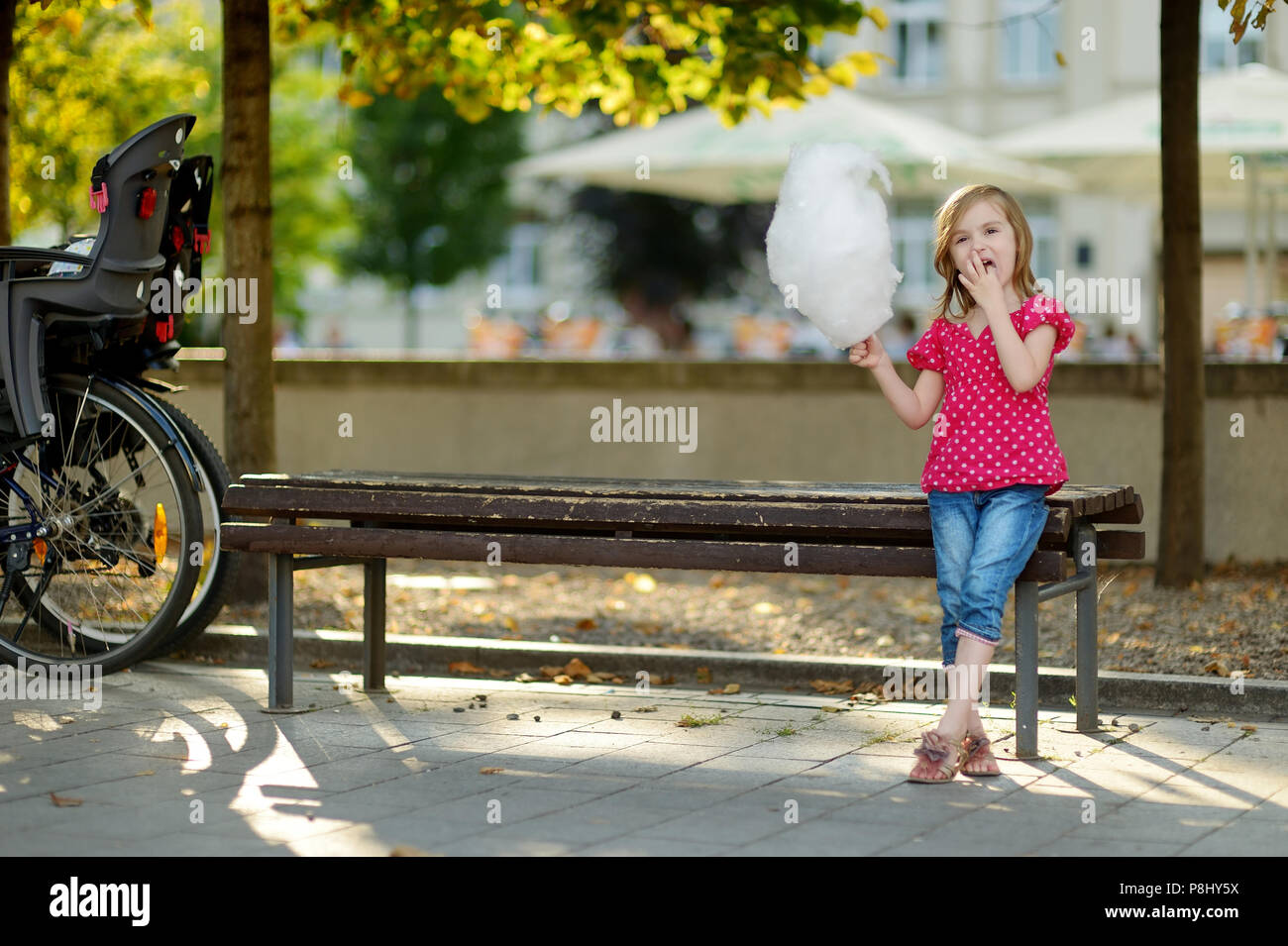 Adorable little girl eating candy-floss outdoors at summer Stock Photo ...