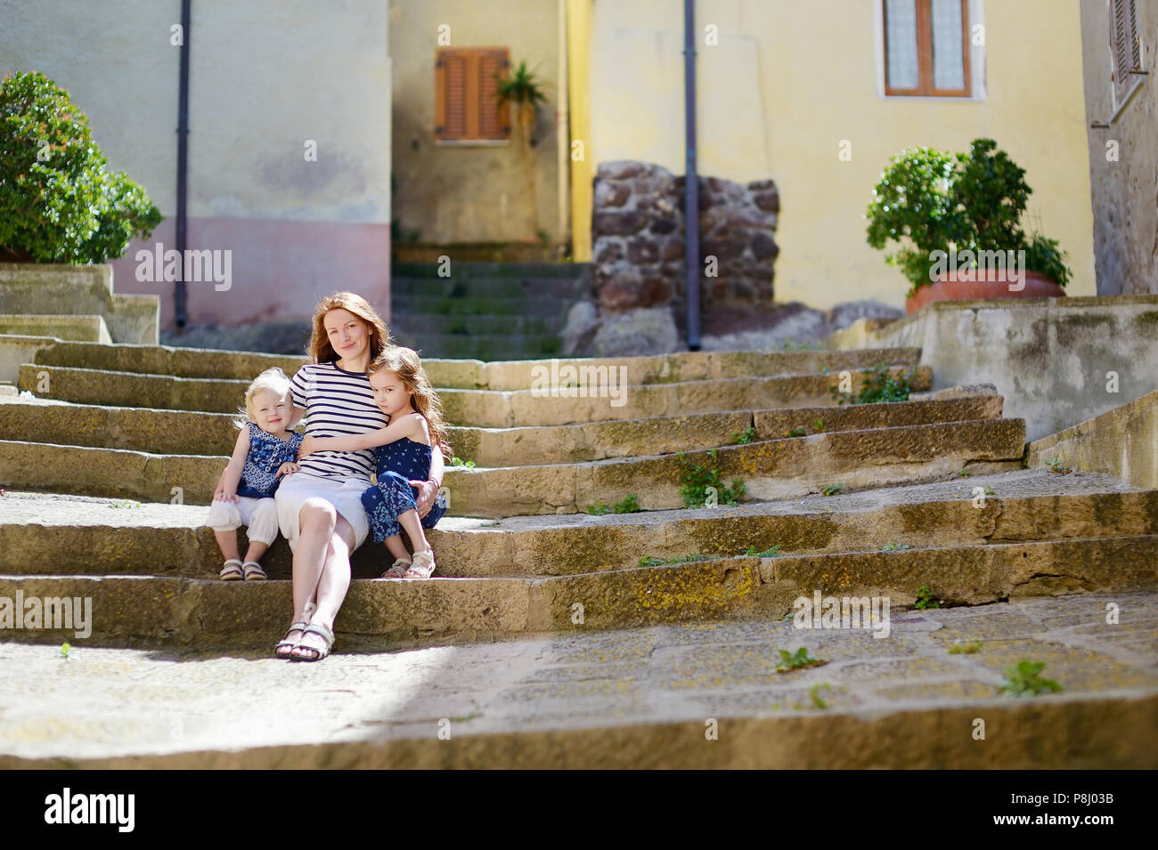 Two cute little sisters and their mother sitting on stairs in italian ...