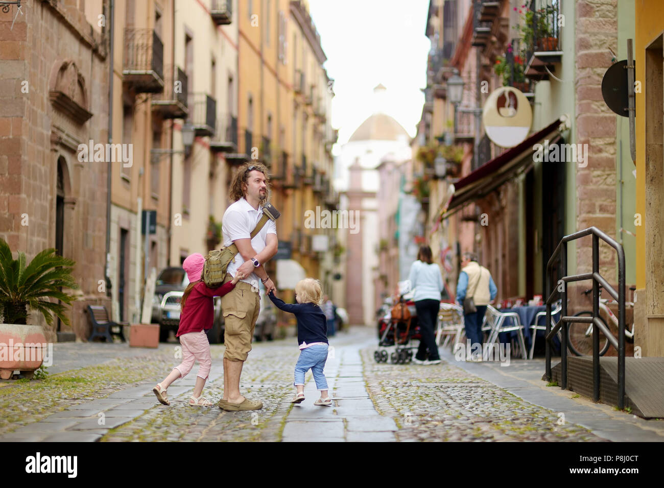 Two little sisters and their father on a street of typical italian town ...