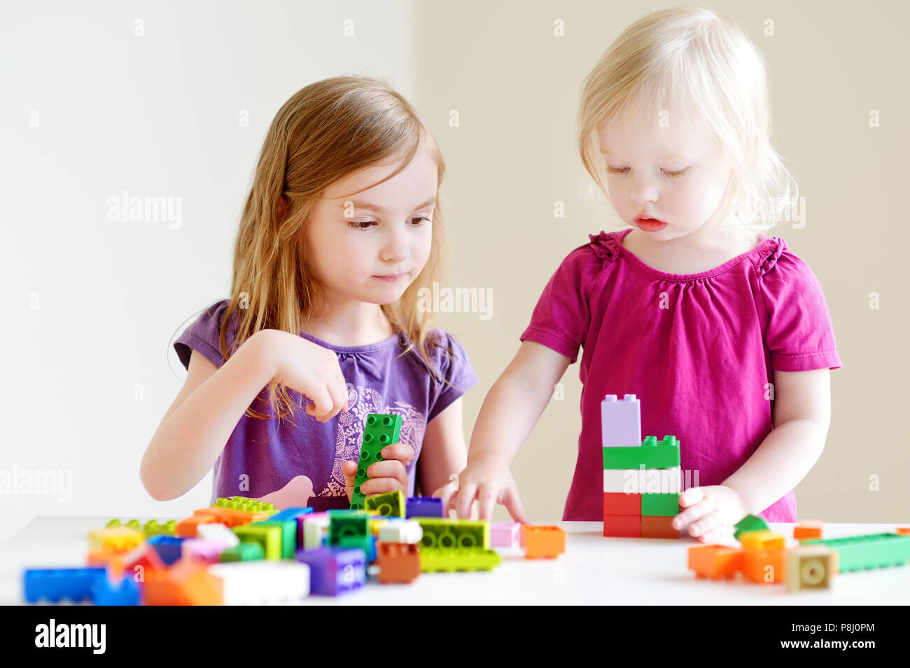 Two cute little sisters playing with colorful plastic blocks at home ...