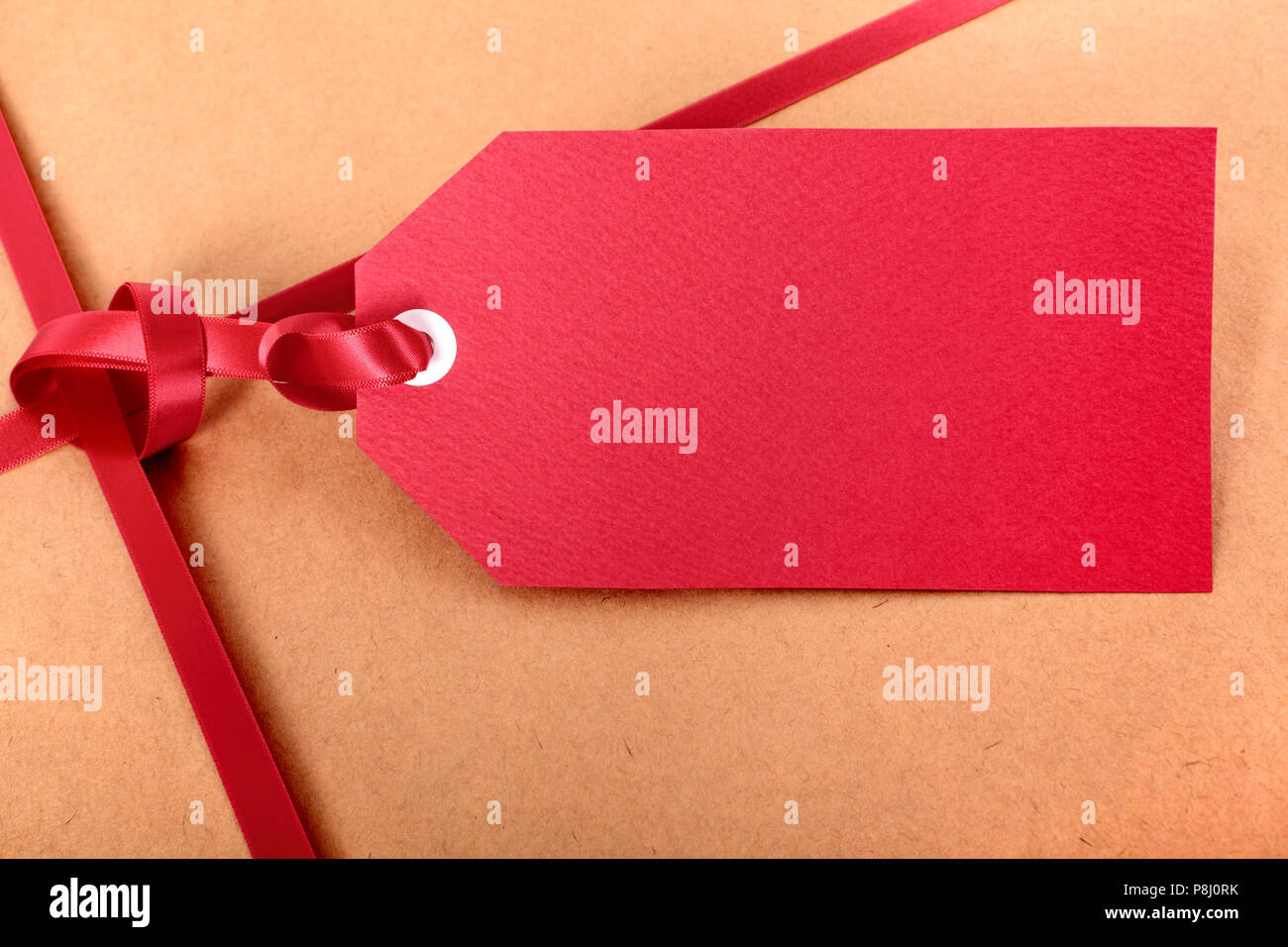 Closeup red gift tag and ribbon, brown parcel wrapping paper background ...