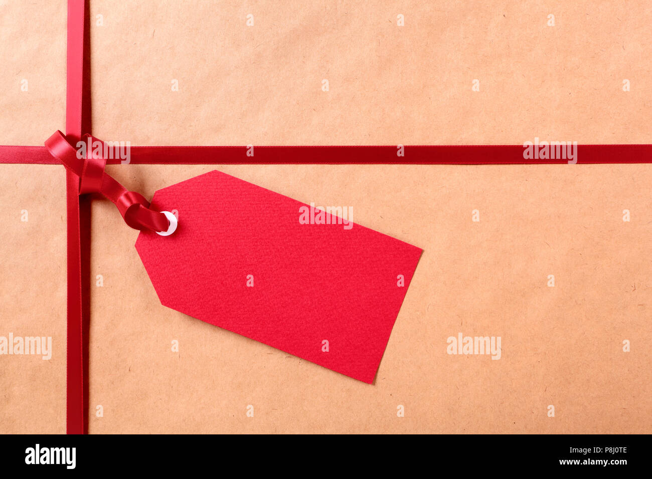 Red gift tag and ribbon, brown parcel wrapping paper background, copy ...