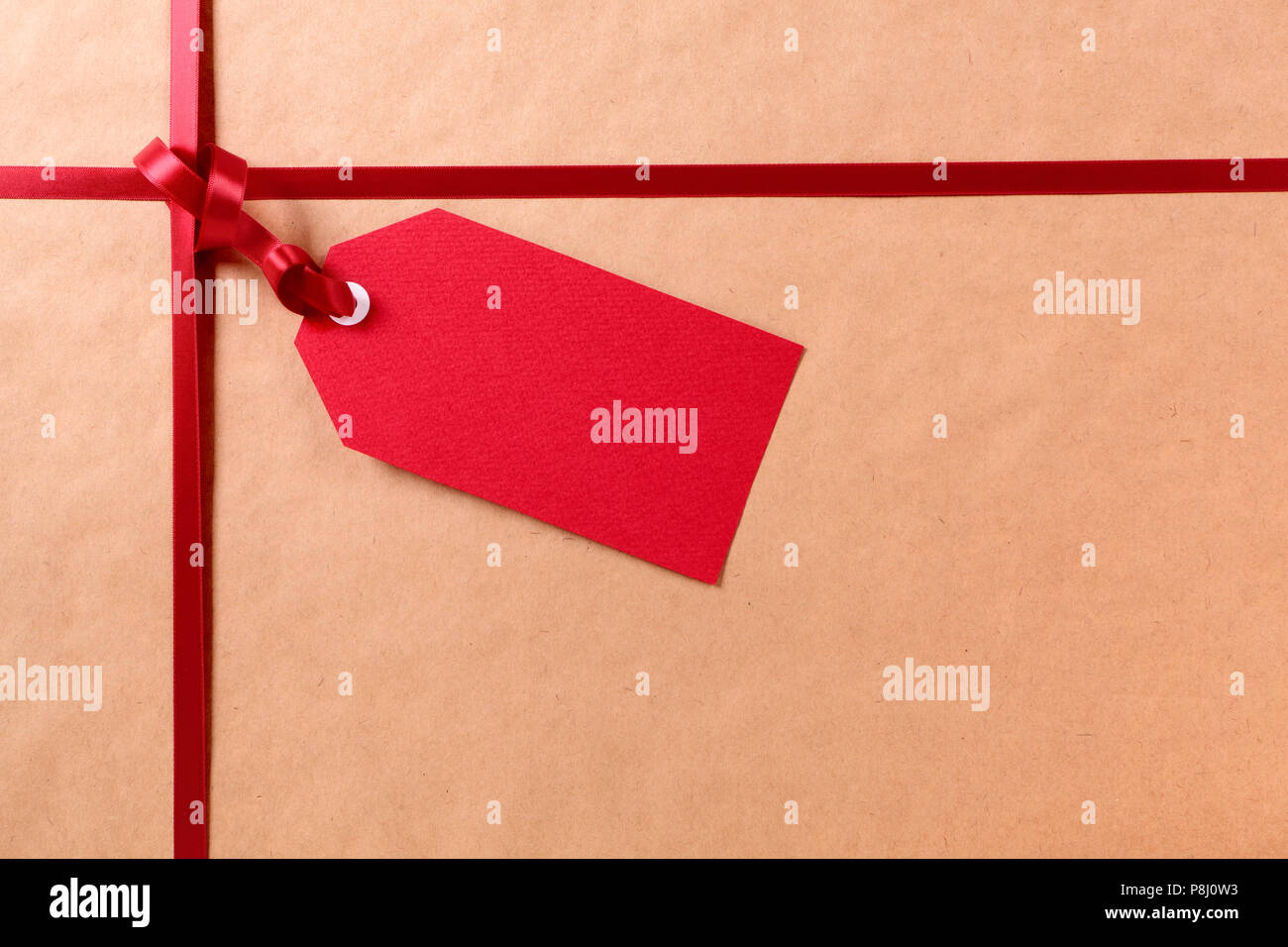 Red gift tag and ribbon, brown parcel wrapping paper background, copy ...