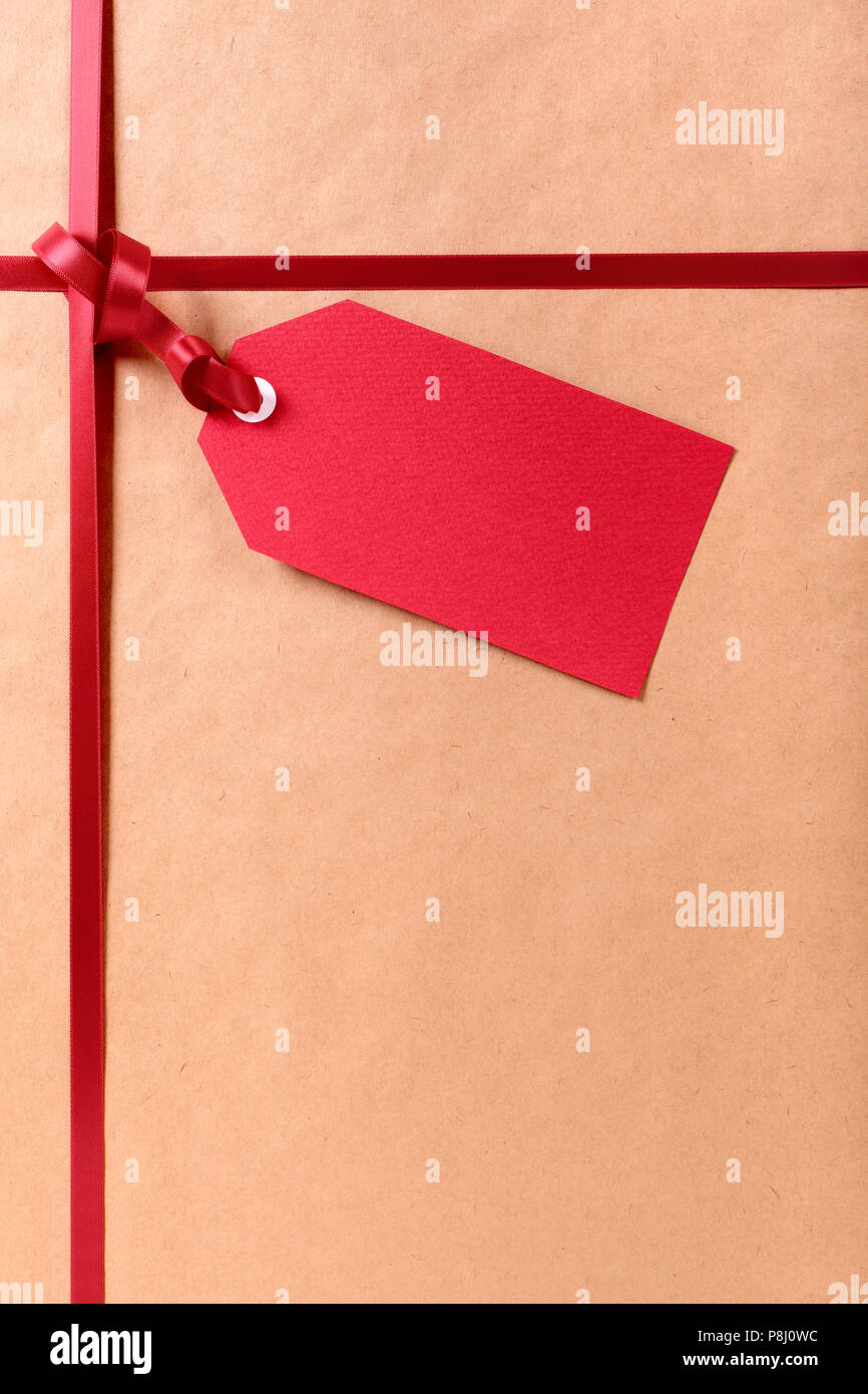 Red gift tag and ribbon, brown parcel wrapping paper background, copy ...