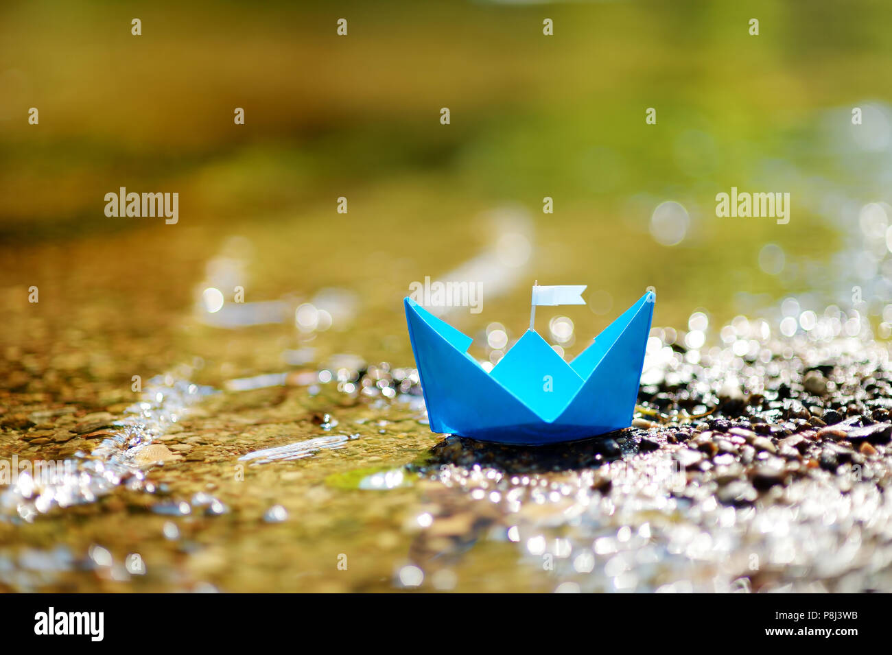 Blue paper boat with a white flag floating on a river Stock Photo - Alamy