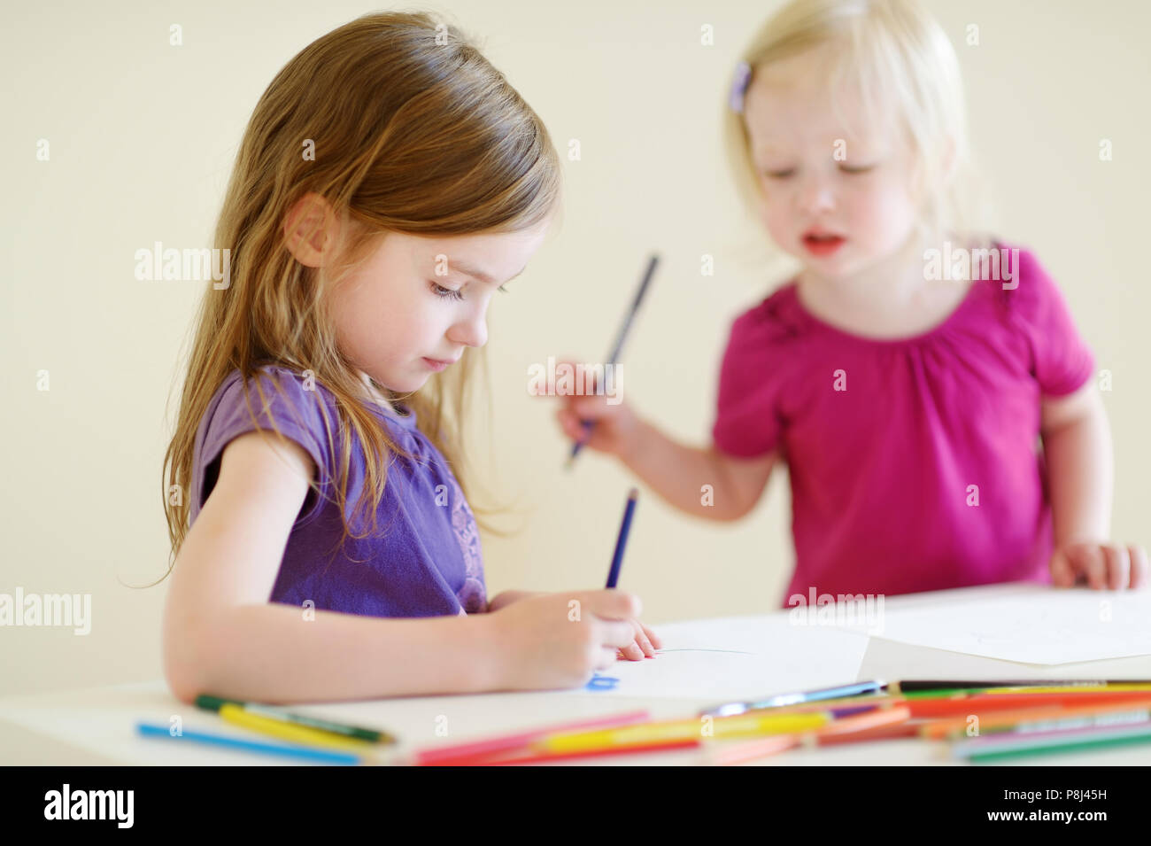 Two cute little sisters drawing with colorful pencils at a daycare ...