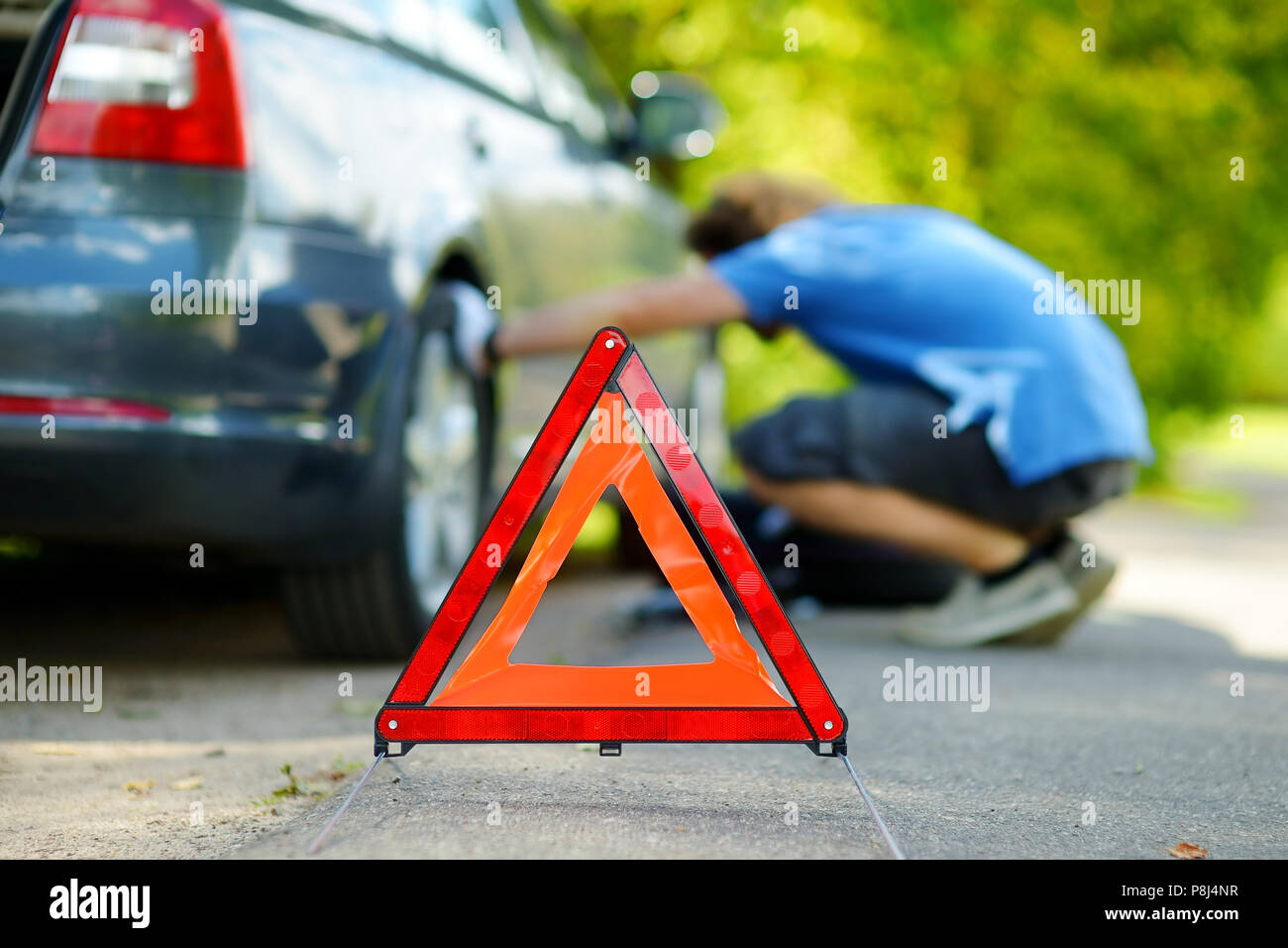 Red warning triangle sign on the road with a man checking his broken ...