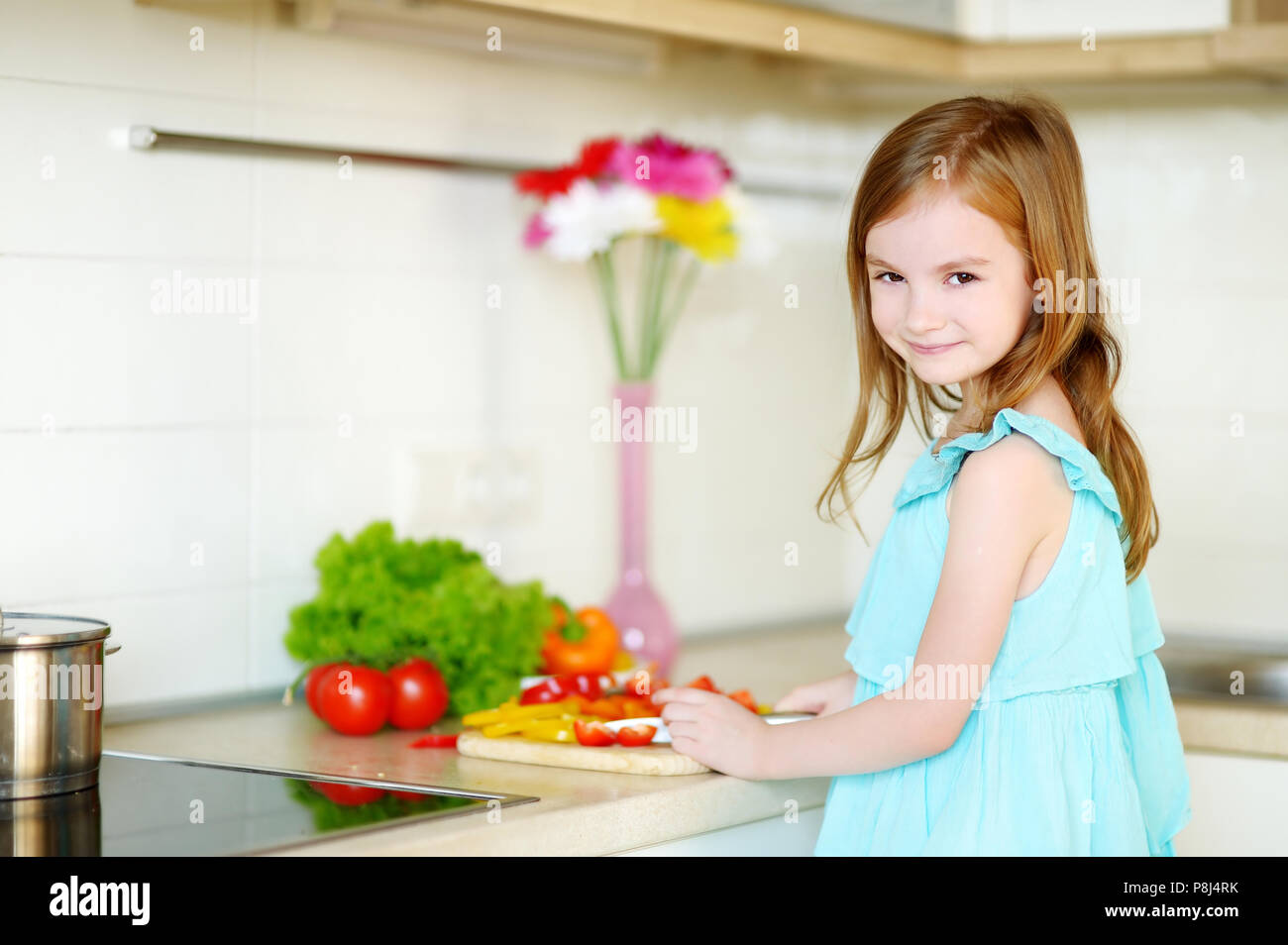Adorable little girl helping her mother to cook dinner in a kitchen ...