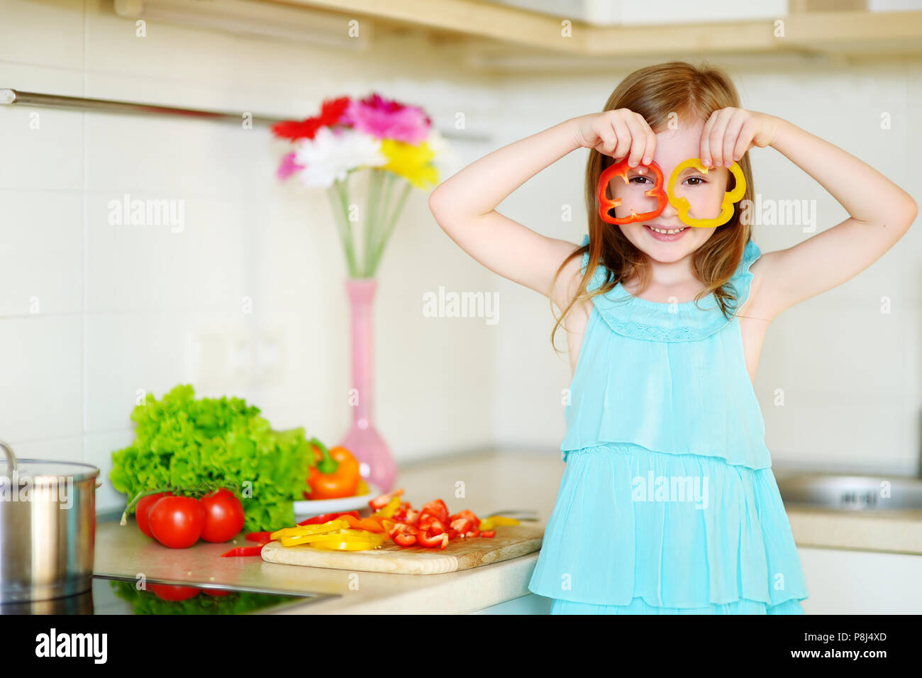 Adorable little girl helping her mother to cook dinner in a kitchen ...