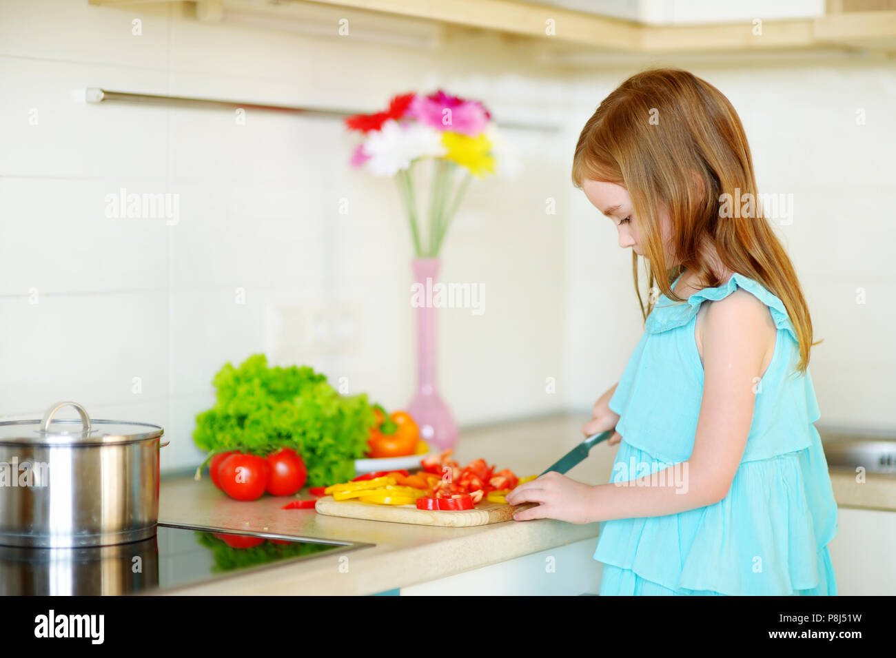 Adorable little girl helping her mother to cook dinner in a kitchen ...