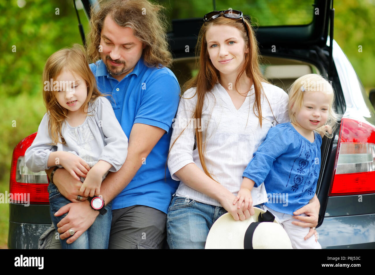Happy family of four sitting in a car just before leaving for a car ...