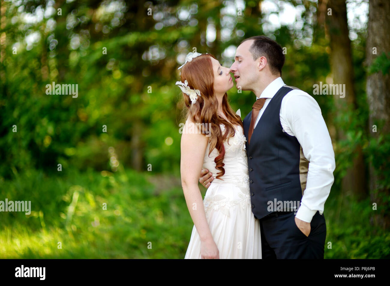 Young bride and groom hugging and kissing in beautiful summer park ...
